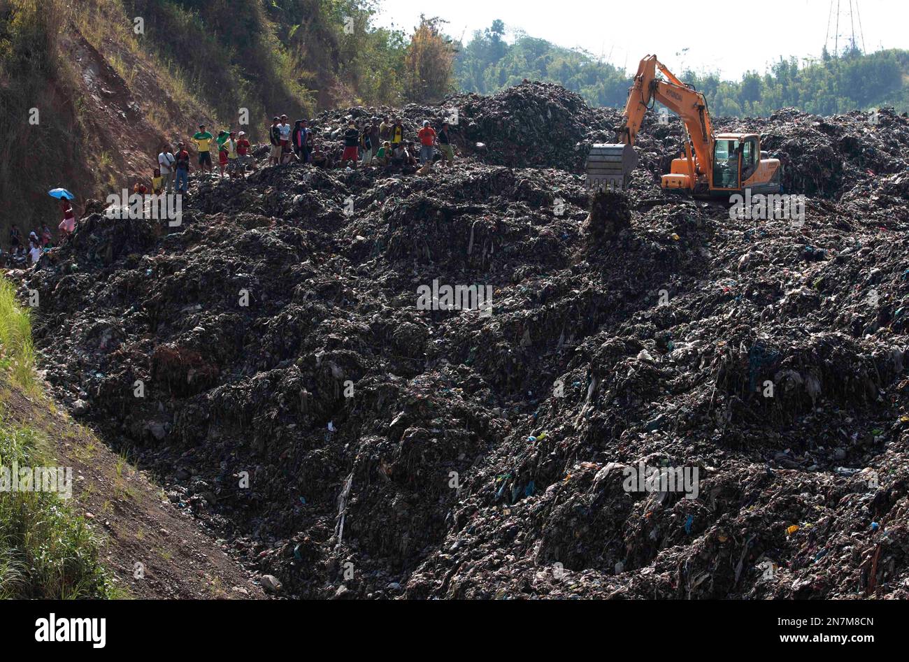 Workers and residents look as backhoe's try to shift through a mountain ...