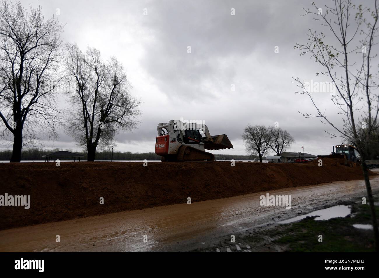 Heavy equipment works atop a temporary levee being quickly constructed ...