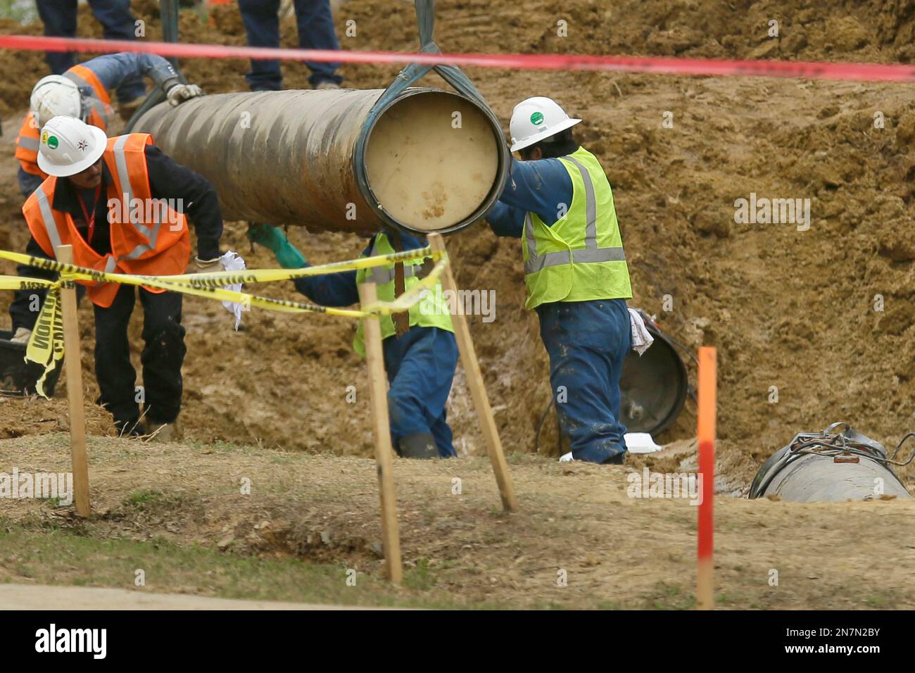Workers guide a damaged section of pipe as it is lifted from an oil ...