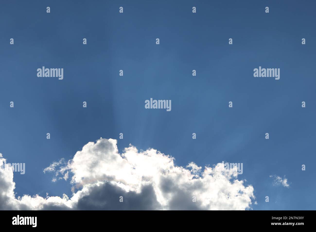 Clouds with light rays coming out of them against a bright blue sky ...
