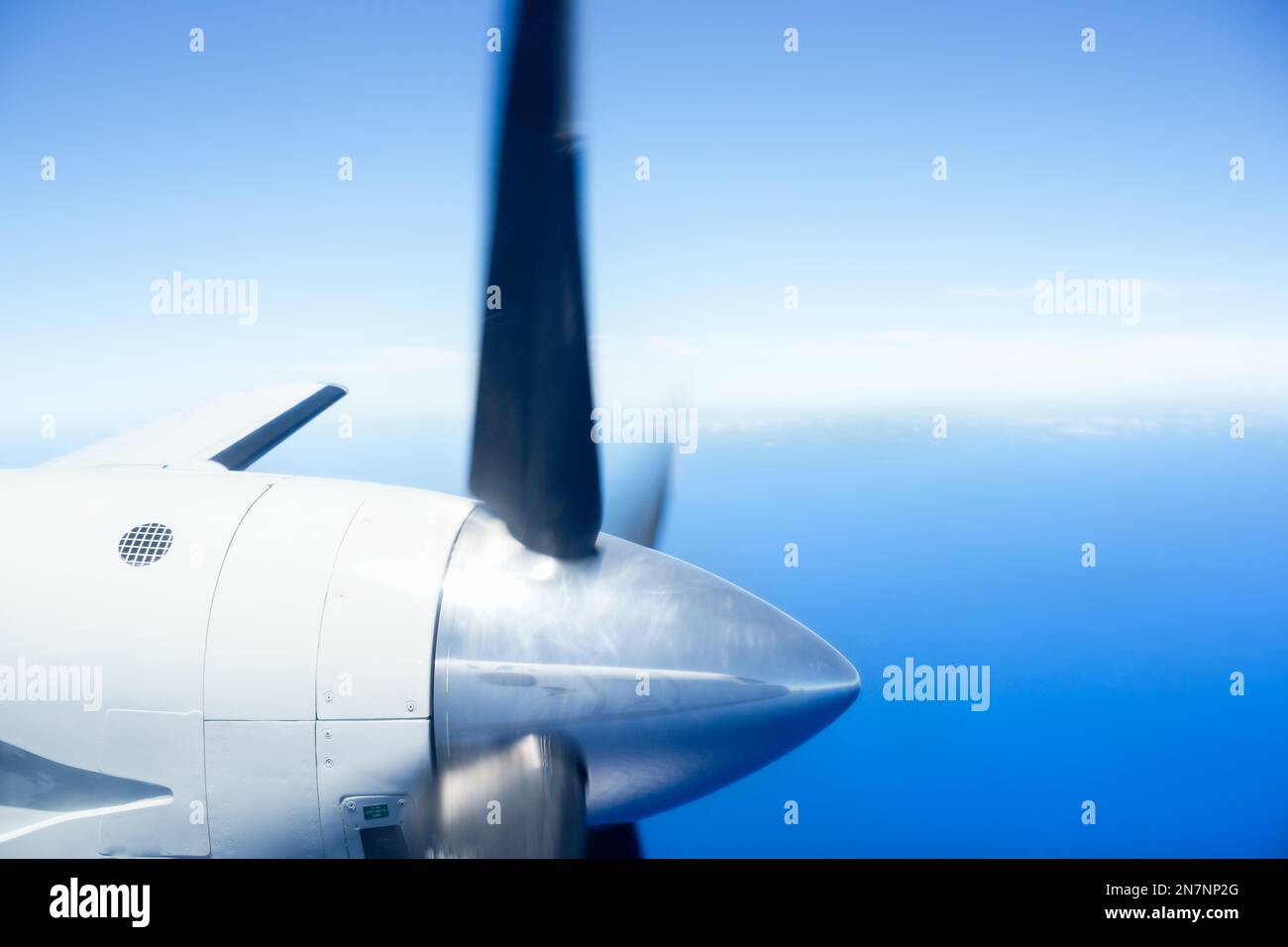 Blue of sky and sea below meet around blurred propeller of airplane ...