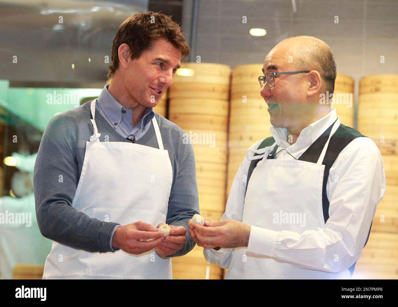 Seen through glass, actor Tom Cruise, left, learns to make dumplings at ...