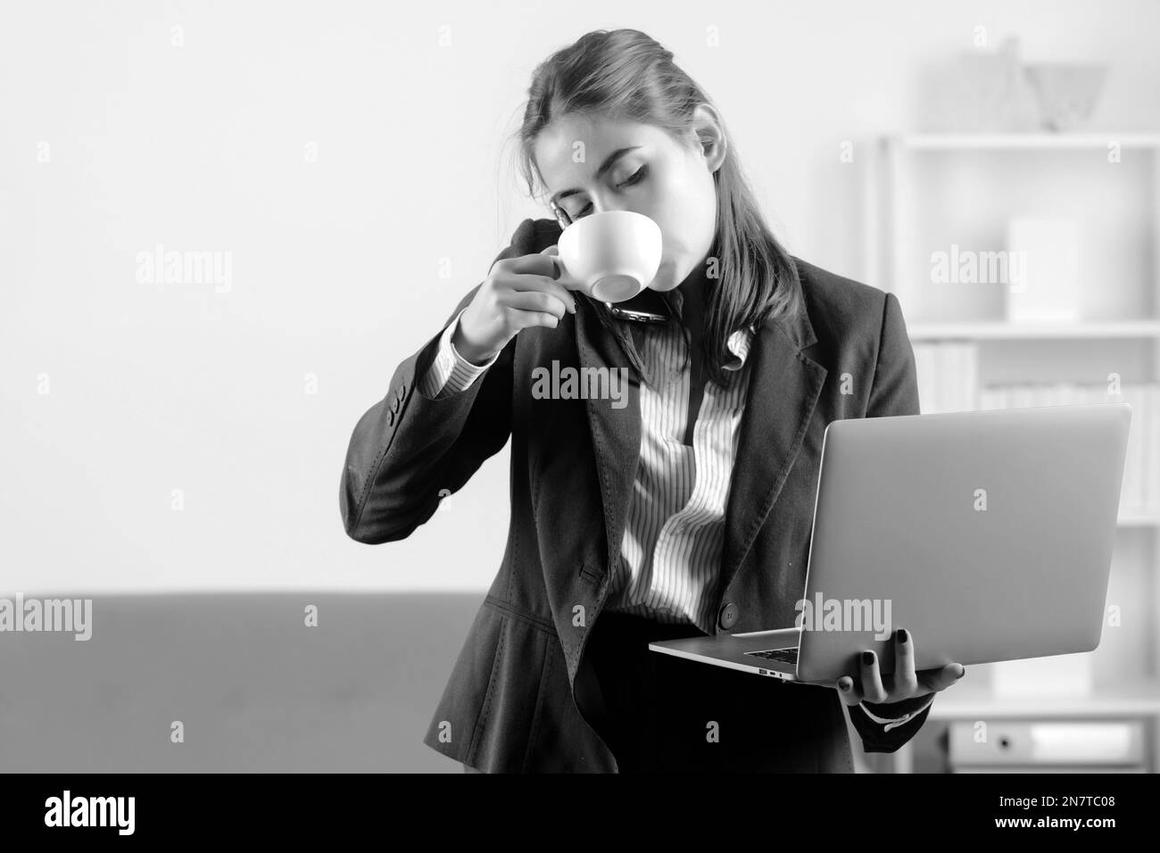 Young businesslady at workplace in the office. Secretary woman in formal wear drinking coffee ...
