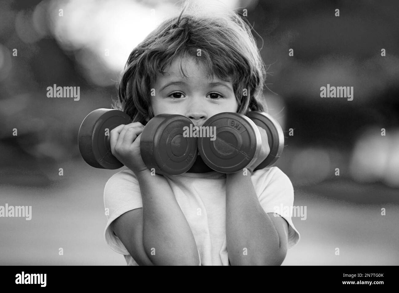 Cute funny little boy doing exercises with dumbbells in green park ...