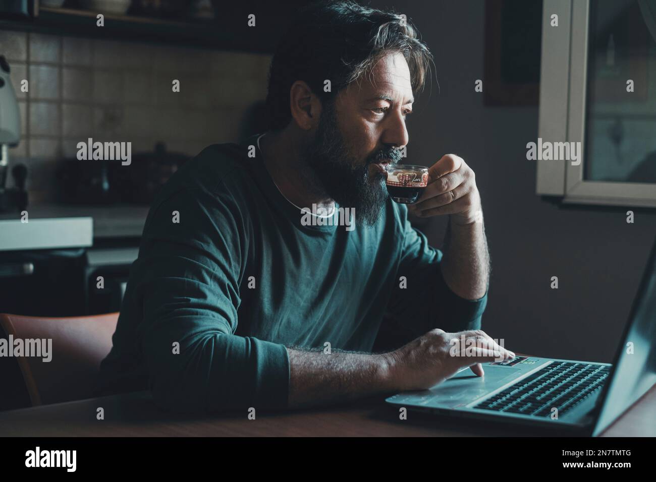 One man alone at home using computer by night in the kitchen and ...