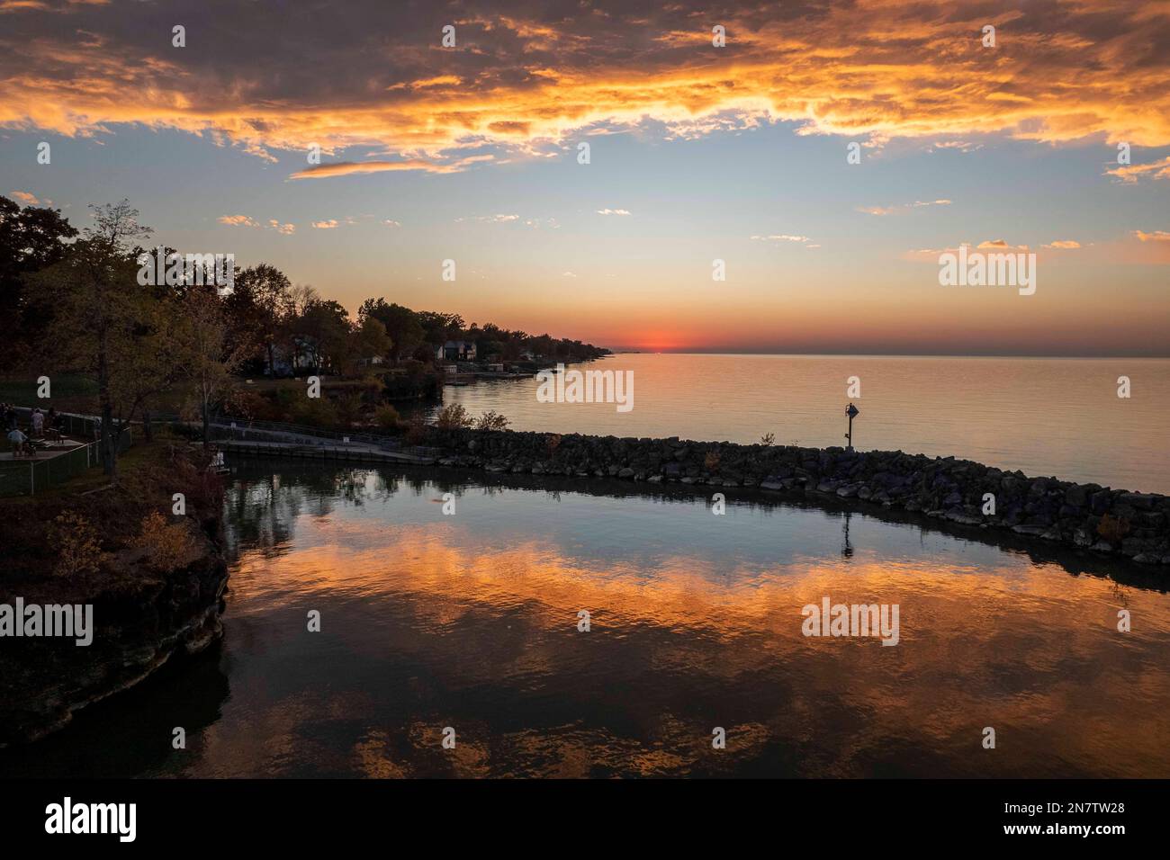 A landscape scene of Sunset sky over trees with reflection on Lake Erie ...