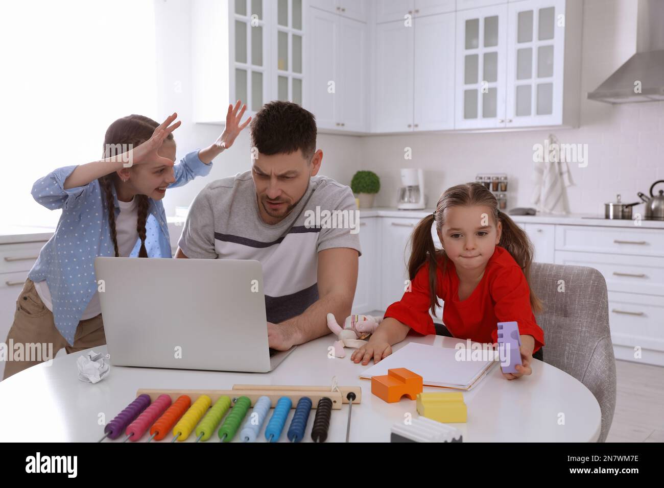 Children disturbing stressed man in kitchen. Working from home during ...