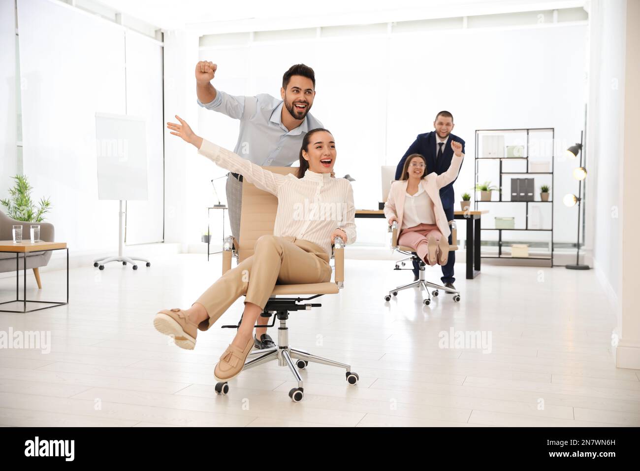 Happy office employees riding chairs at workplace Stock Photo - Alamy