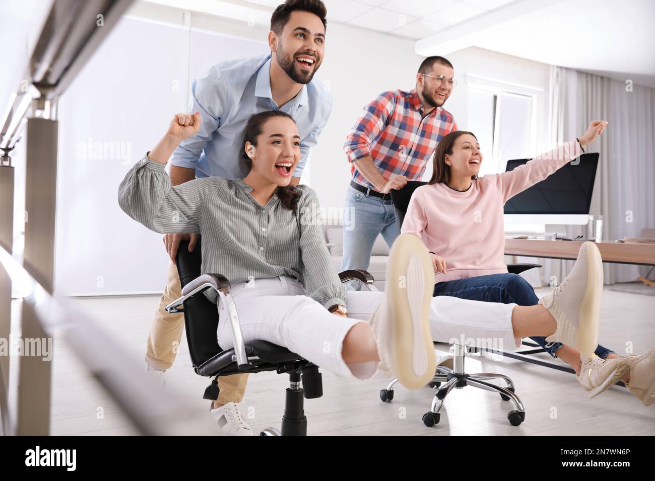 Happy office employees riding chairs at workplace Stock Photo - Alamy