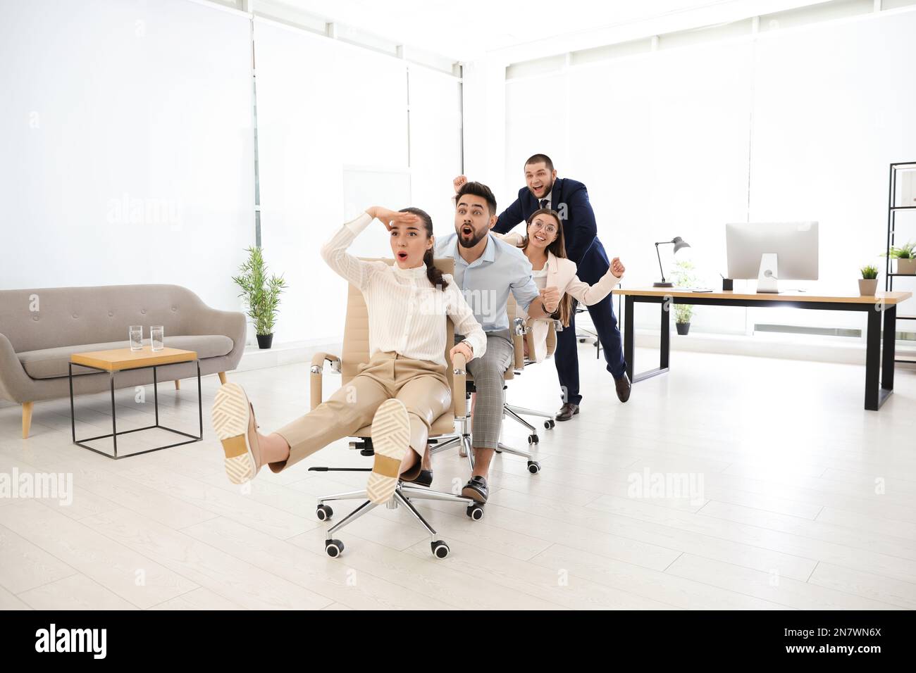 Happy office employees riding chairs at workplace Stock Photo - Alamy