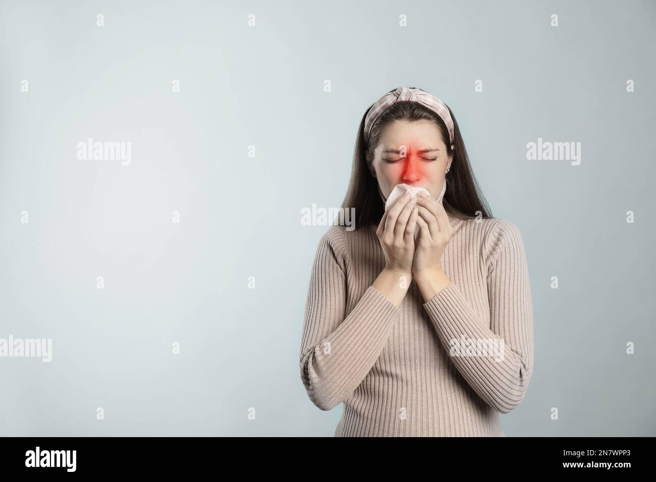 Young woman with tissue suffering from runny nose on light background ...