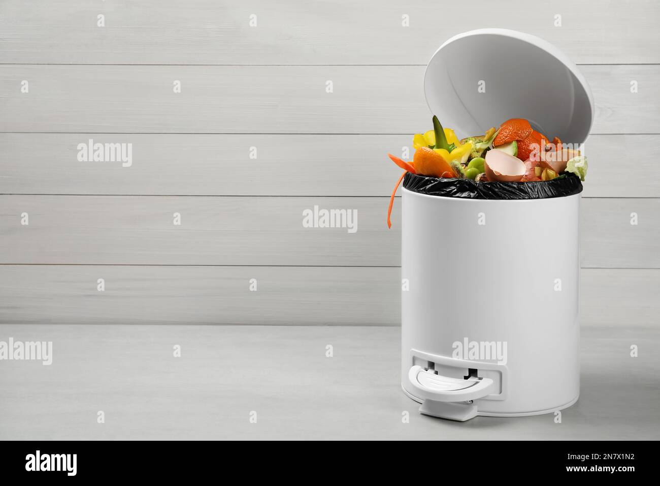 Trash bin with natural garbage on light background, space for text ...