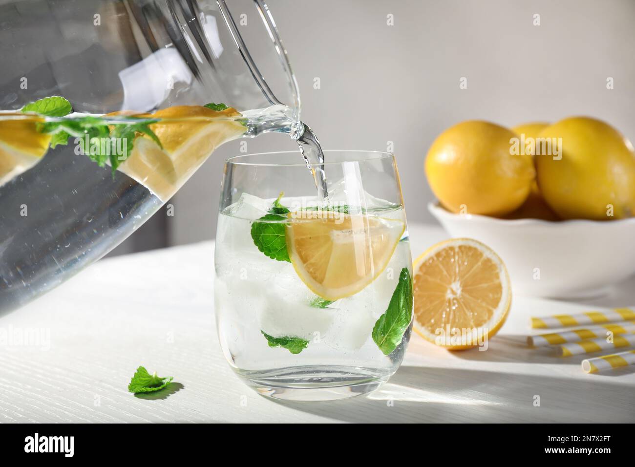 Pouring of refreshing lemonade into glass on white table Stock Photo ...