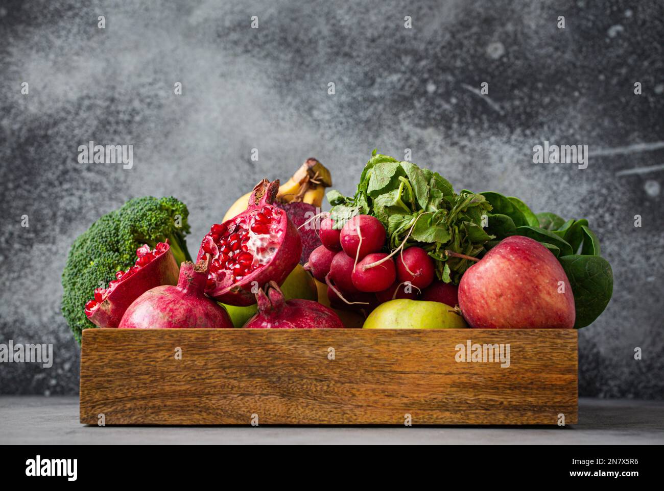 Selection of fresh fruit, greens, vegetables in wooden tray on grey ...