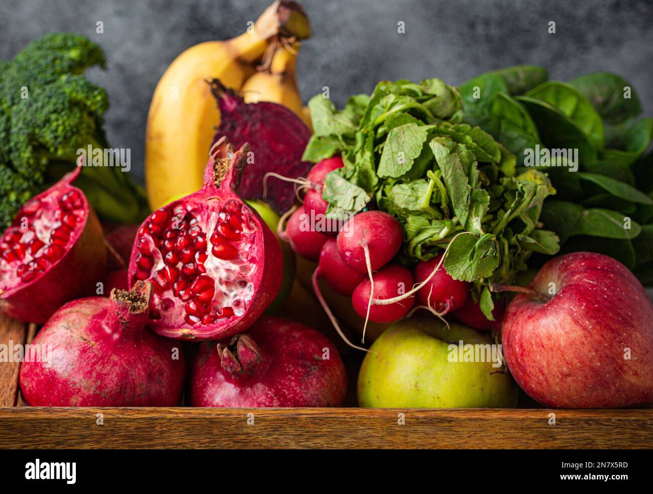 Selection of fresh fruit, greens, vegetables in wooden tray on grey ...