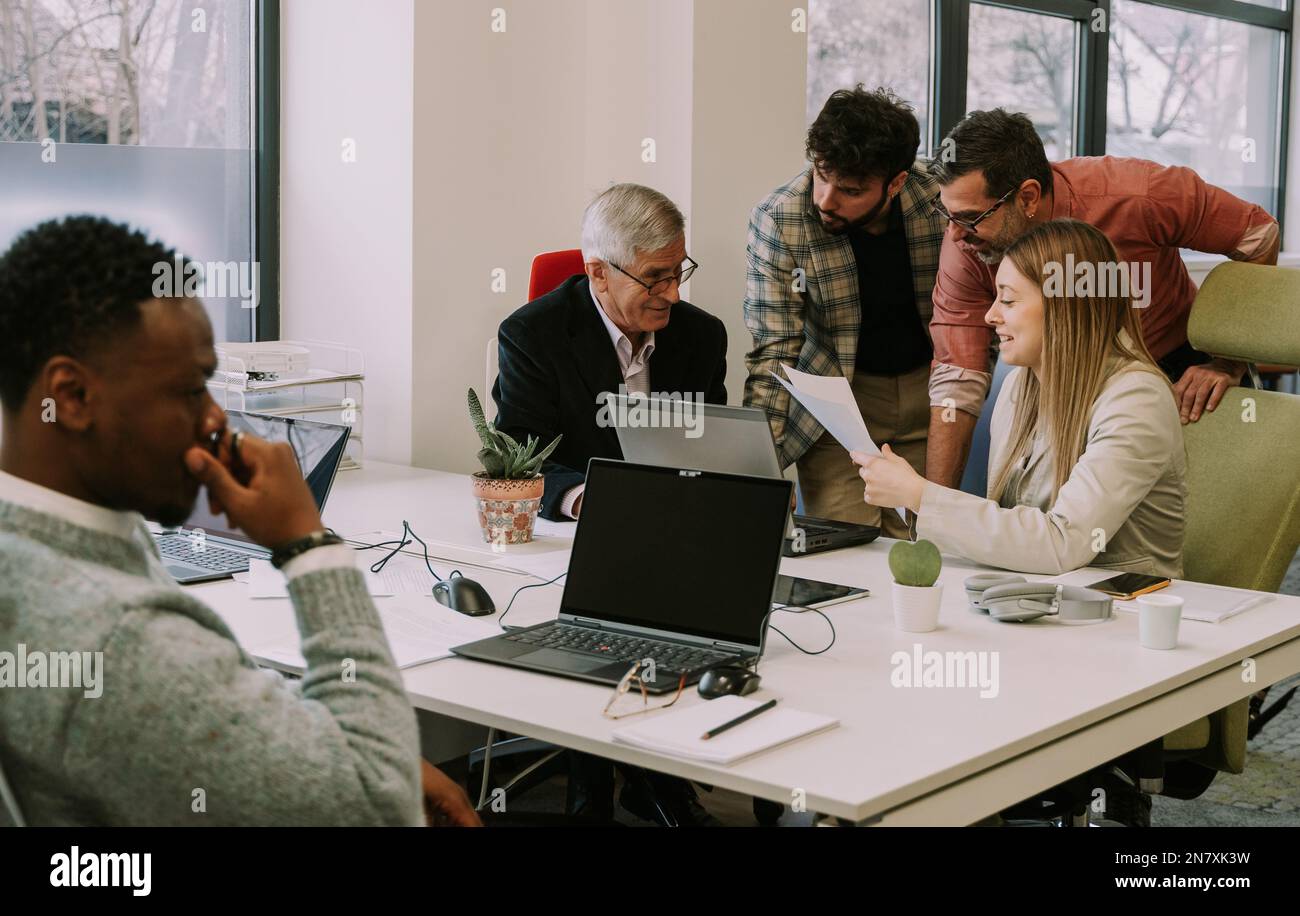 Four colleagues working and having fun conversation. Their coworker is ...
