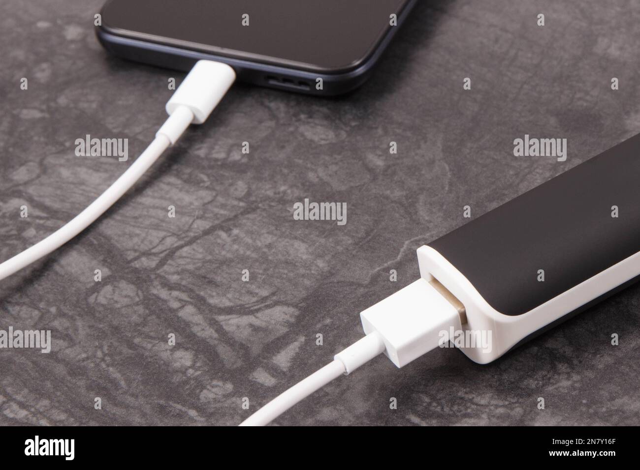 Black smartphone with connected white plug of external powerbank ...