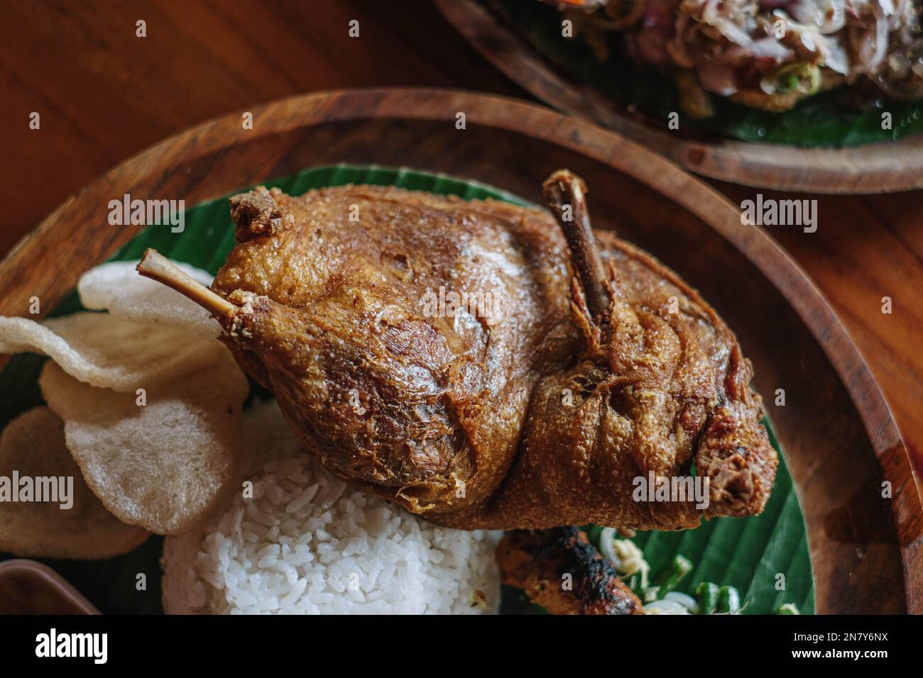A wooden plate of deep-fried duck with rice, vegetables, chili and ...