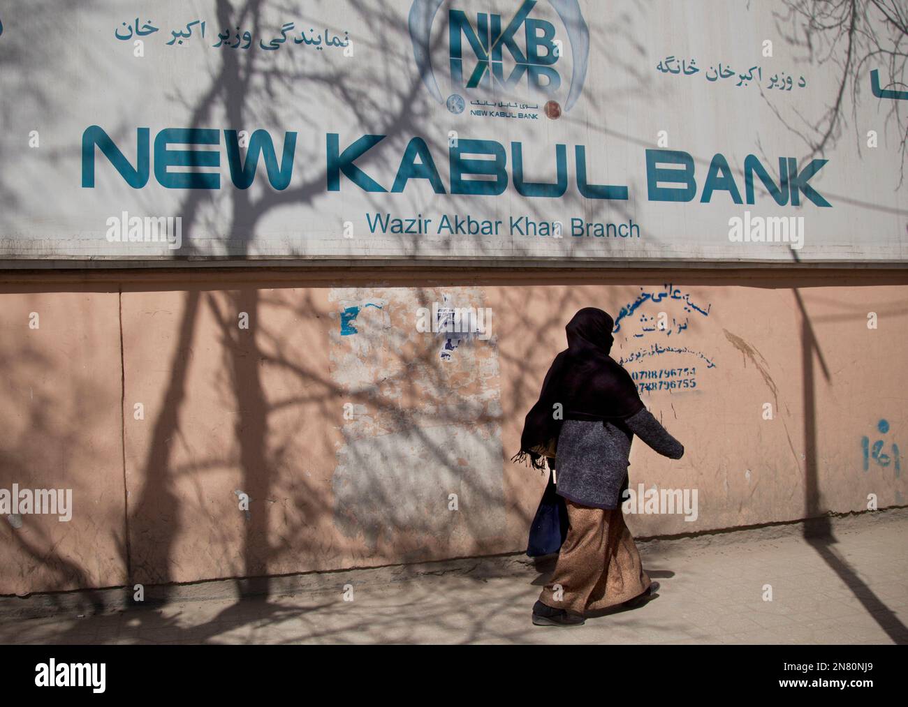 An Afghan woman passes by a sign of the New Kabul Bank in the center of ...