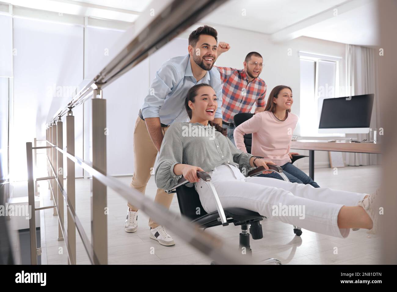Happy office employees riding chairs at workplace Stock Photo - Alamy