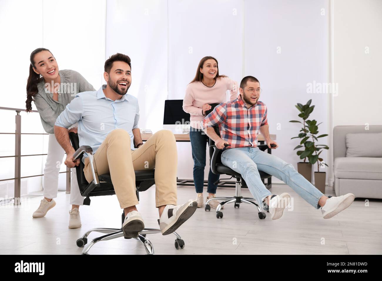 Happy office employees riding chairs at workplace Stock Photo - Alamy