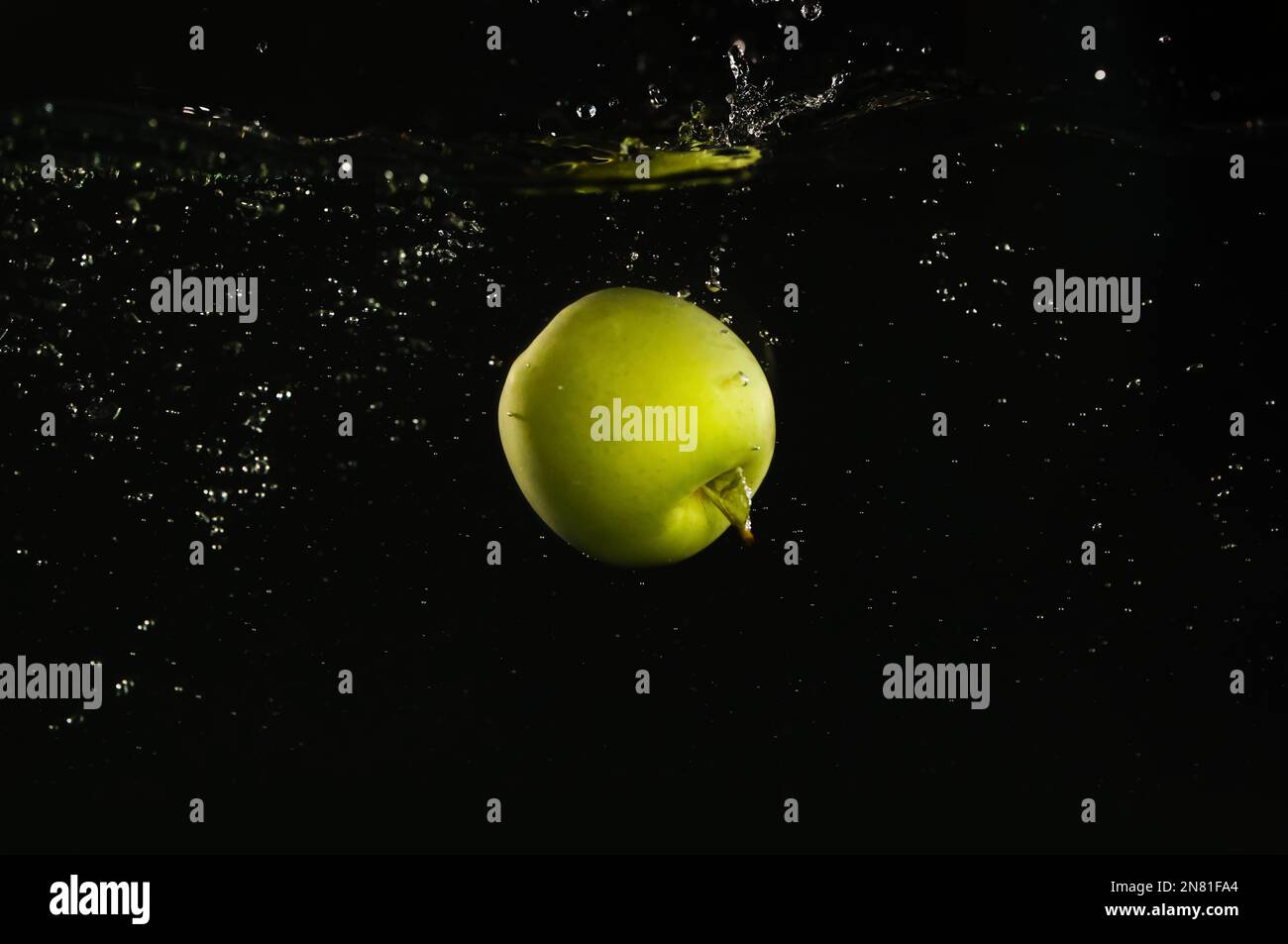 Green apple falling down into clear water against black background ...
