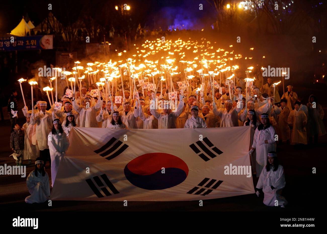 South Koreans, wearing traditional Korean costumes, carry torches and a ...