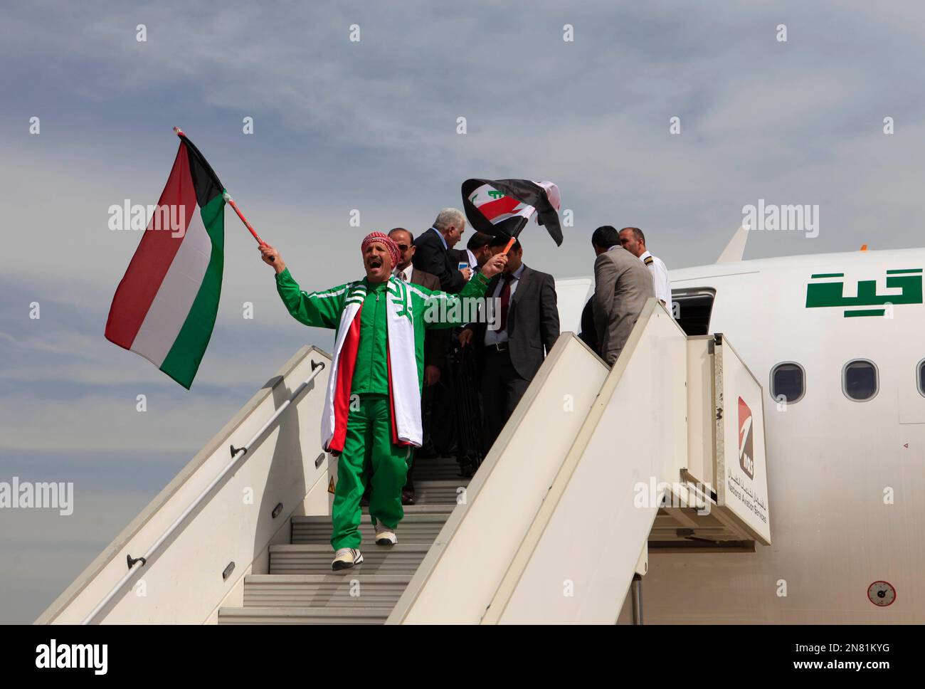 Passengers disembark from an Iraqi Airways plane as a man waves Iraq ...