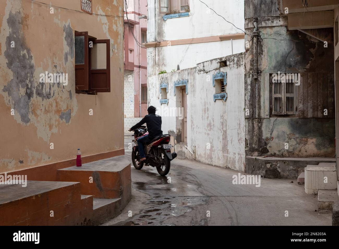 Diu, India - December 2018: A man riding a motorbike in a narrow alley ...