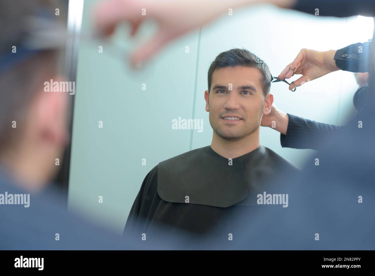 handsome man is smiling while having his hair cut Stock Photo - Alamy