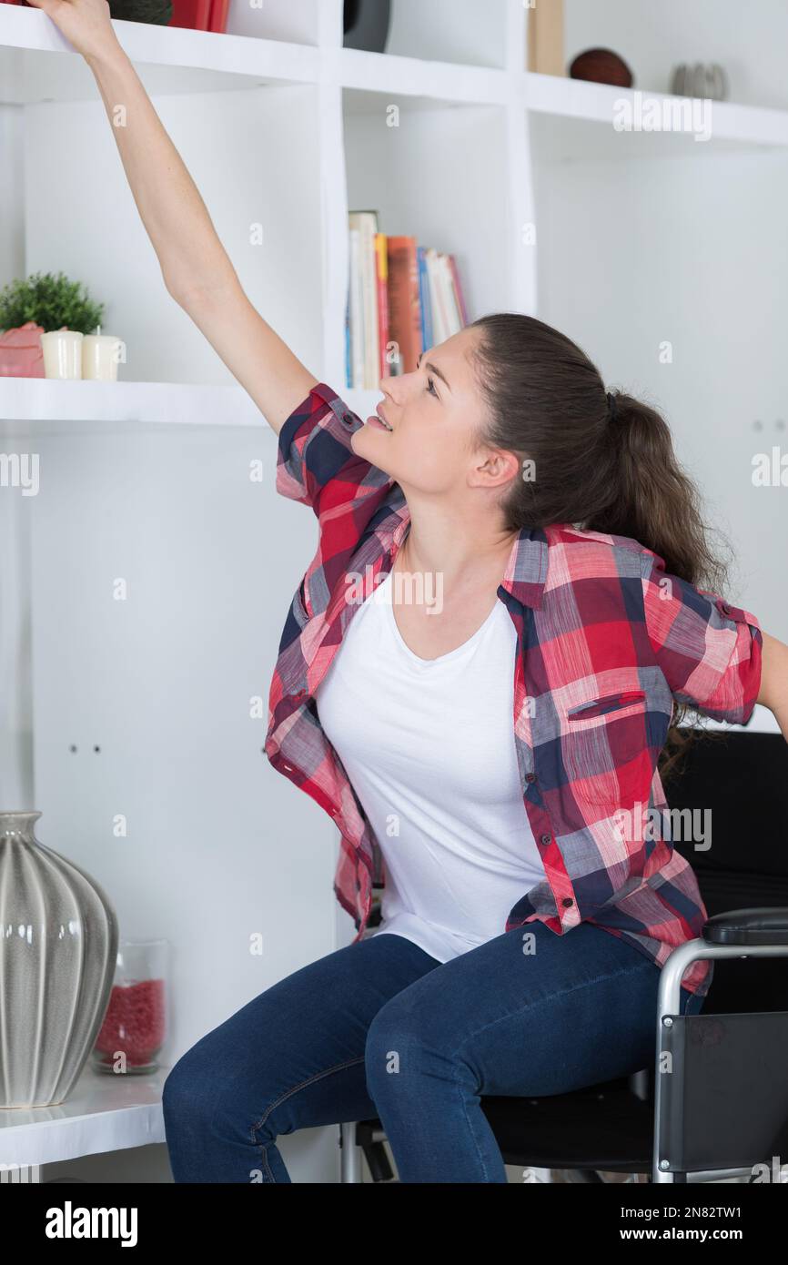 wheelchair boung girl reaching for book from high shelf Stock Photo - Alamy