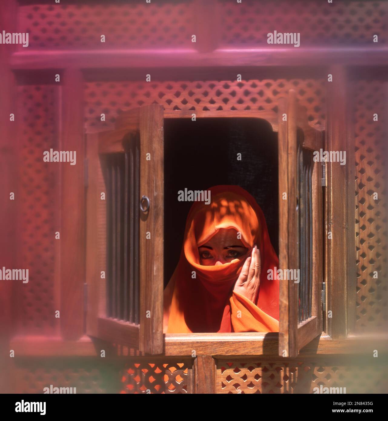 woman with orange color veil looking out of half open wooden window ...