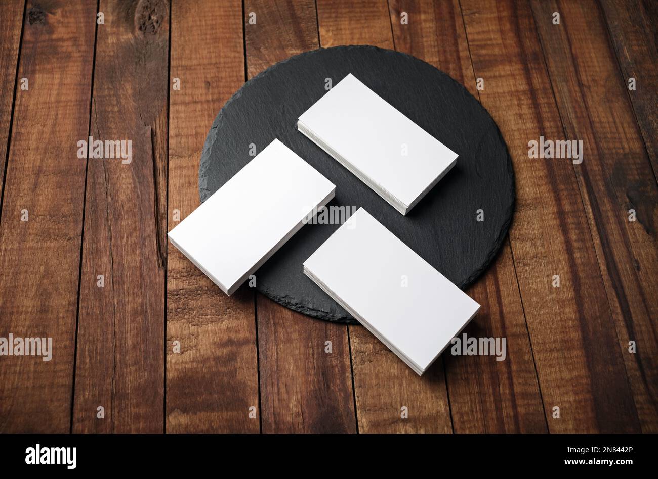 Three blank business cards and round slate plate on wooden background ...