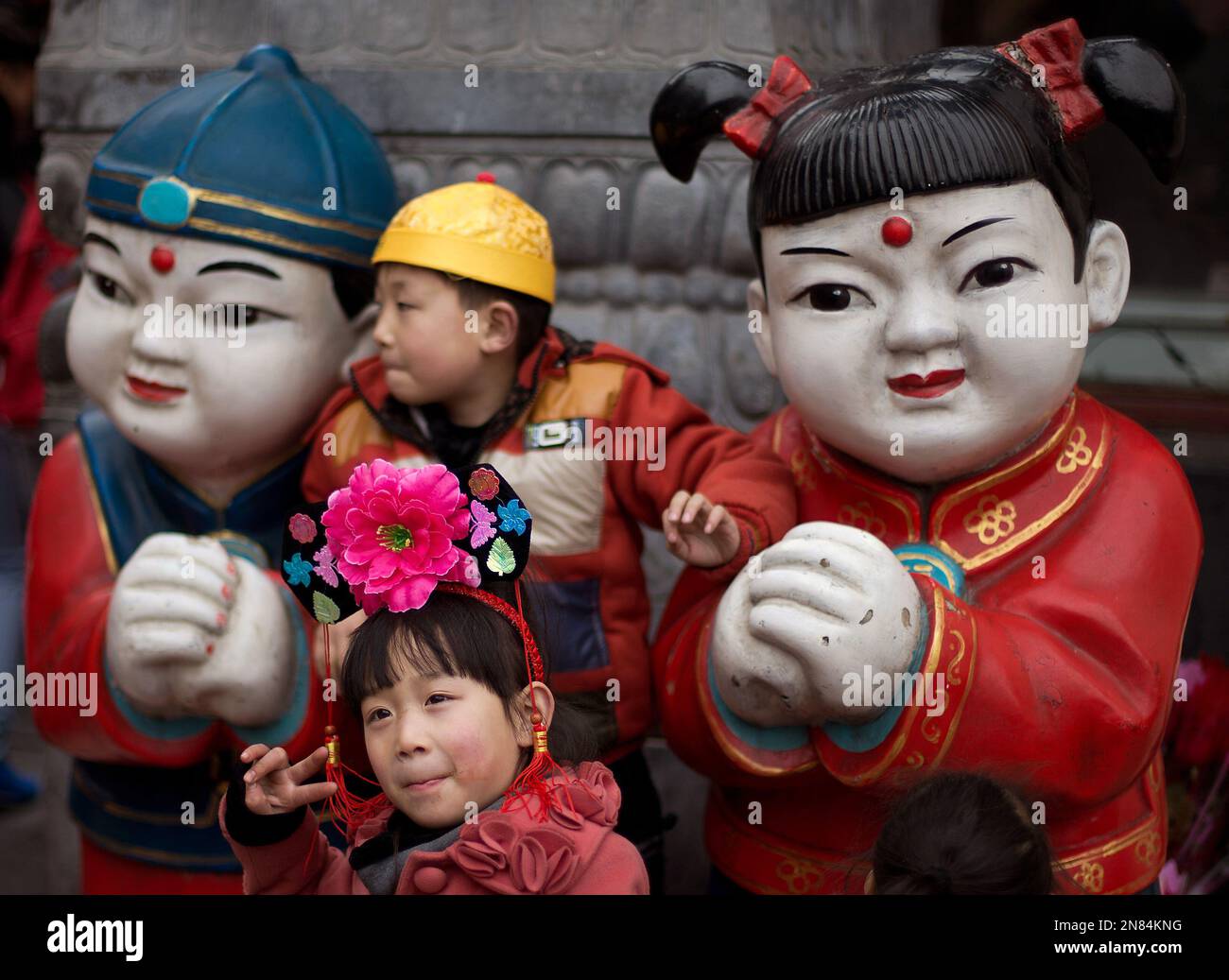 Children wearing traditional Chinese hats pose with a pair of statues ...