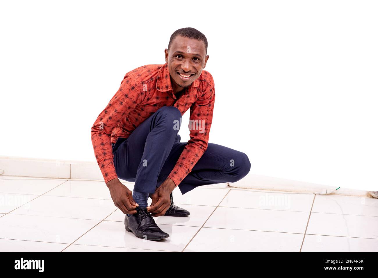 a handsome businessman in a checkered shirt crouching on a white background adjusting his laces ...