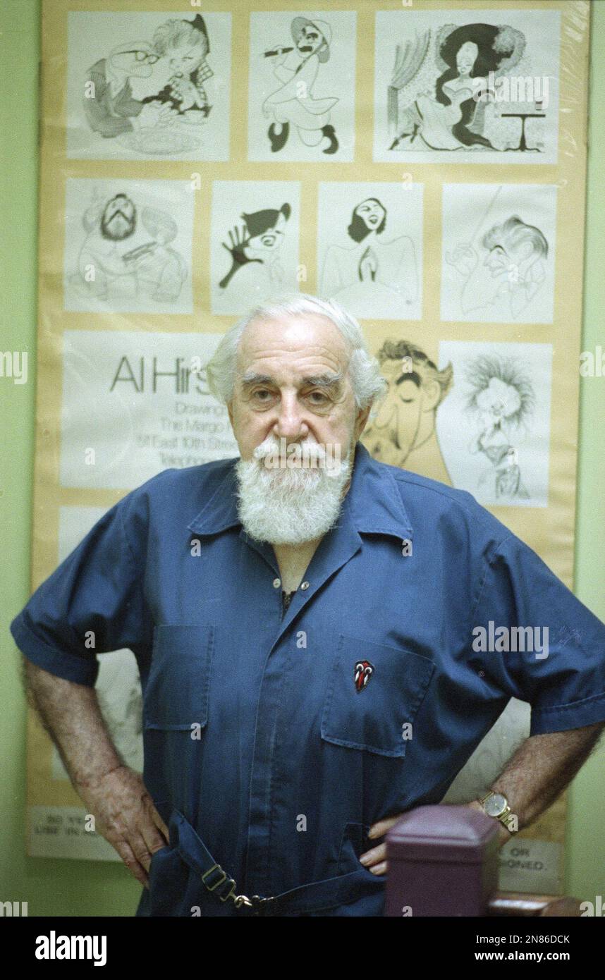 Artist Al Hirschfeld stands in front of a collection of his famous ...
