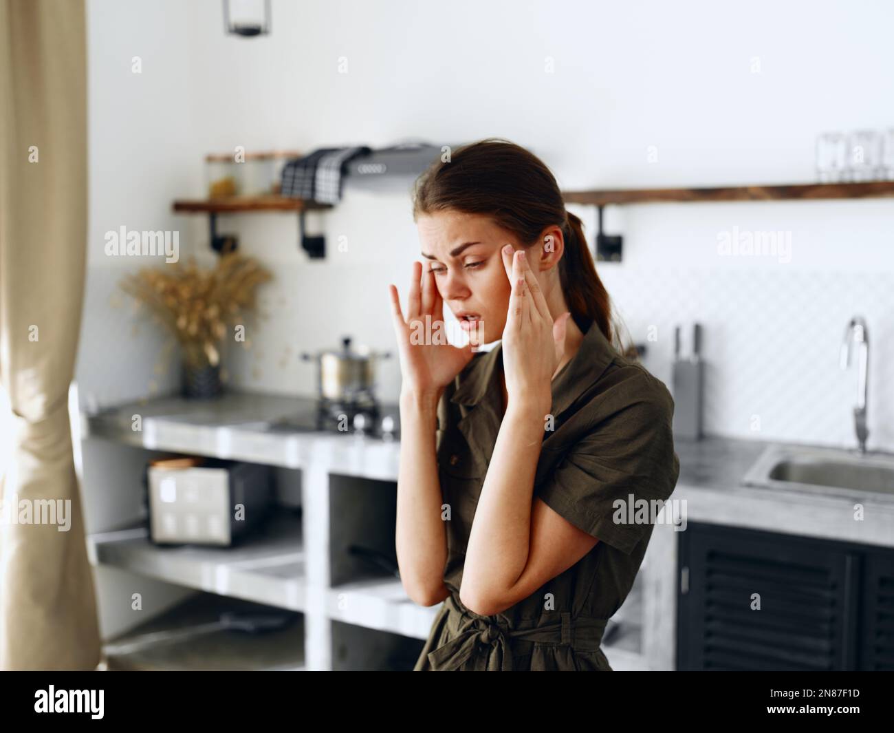 Portrait of a sad tired woman with a sore head in the kitchen, domestic ...