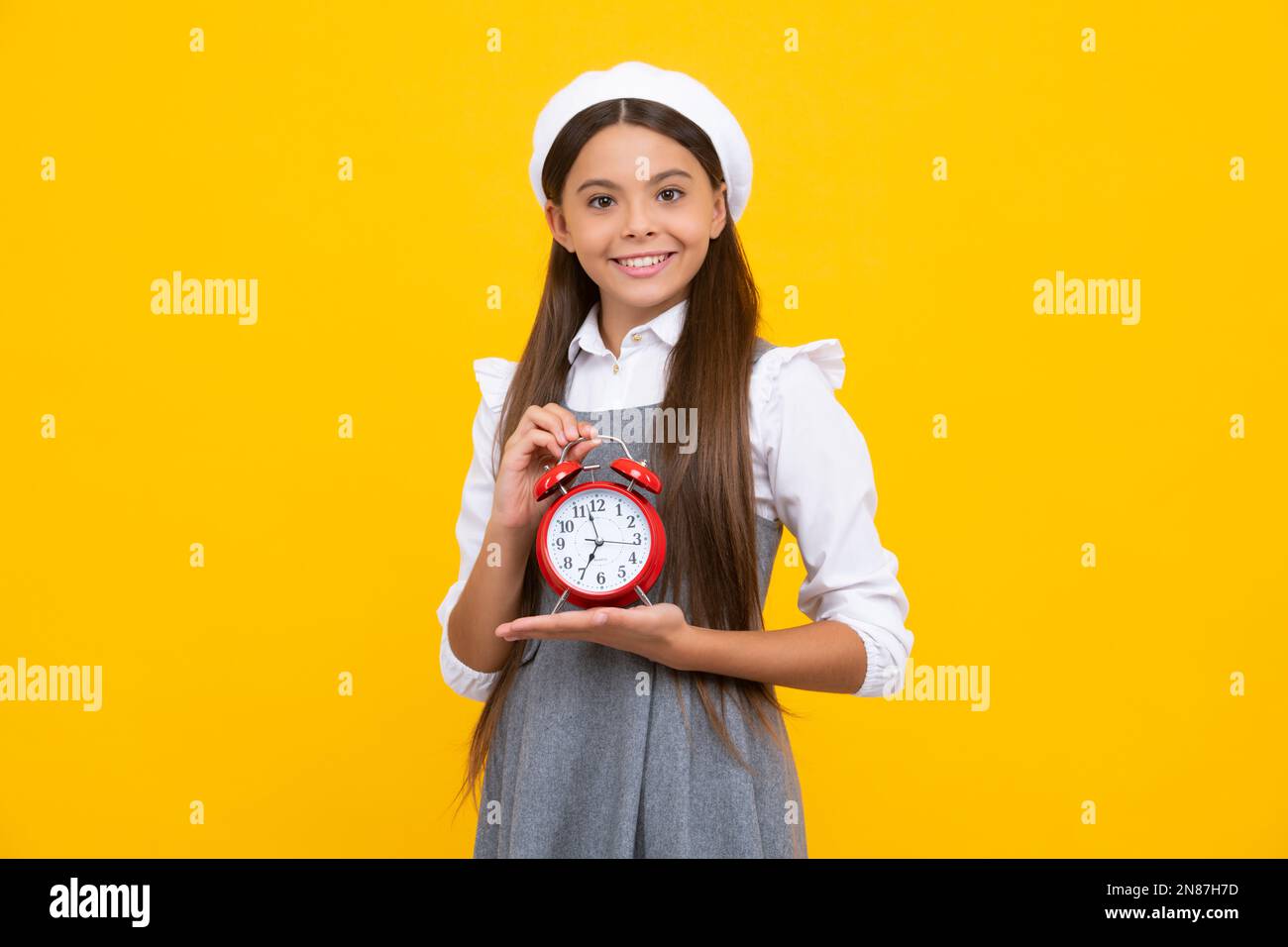 Child teenager girl with alrm clock isolated on yellow background. Time ...