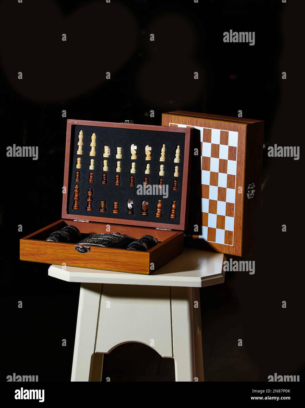 Small wooden chess set alongside a black flask on a white table with ...