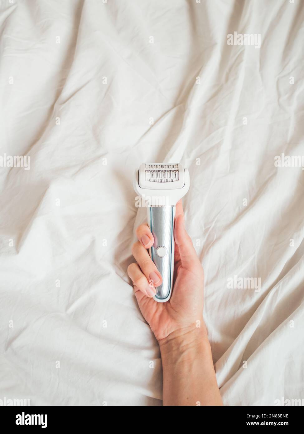 Woman holds epilator on crumpled bed background. Epilation ...