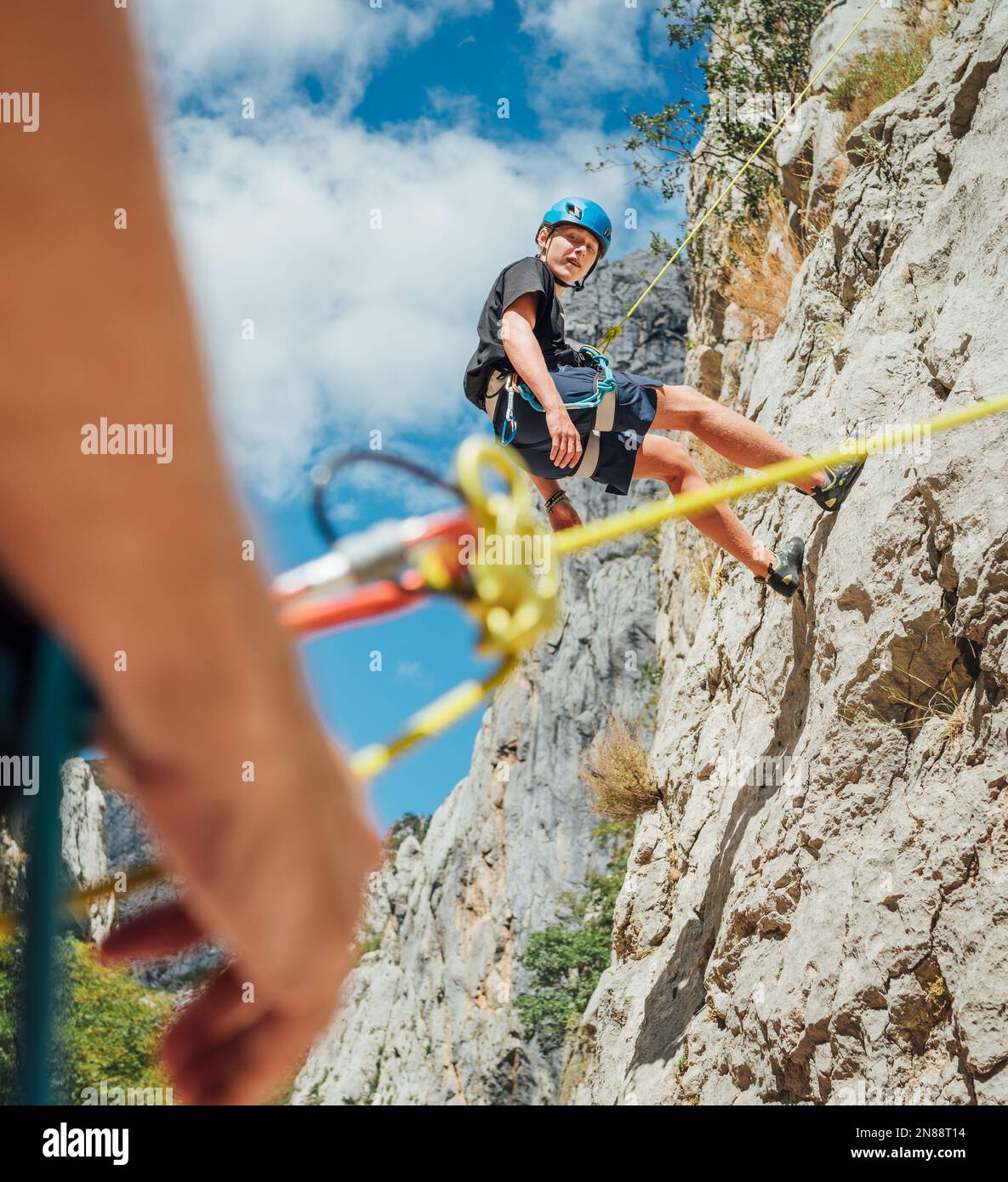 Teenager boy on the natural cliff climbing wall. Boy hanging on a rope ...