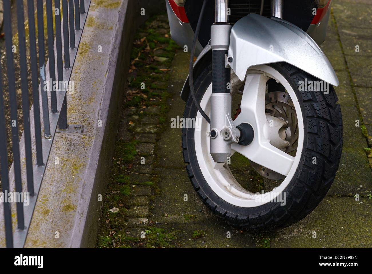 The front wheel of a motor scooter standing on the sidewalk. Close up ...