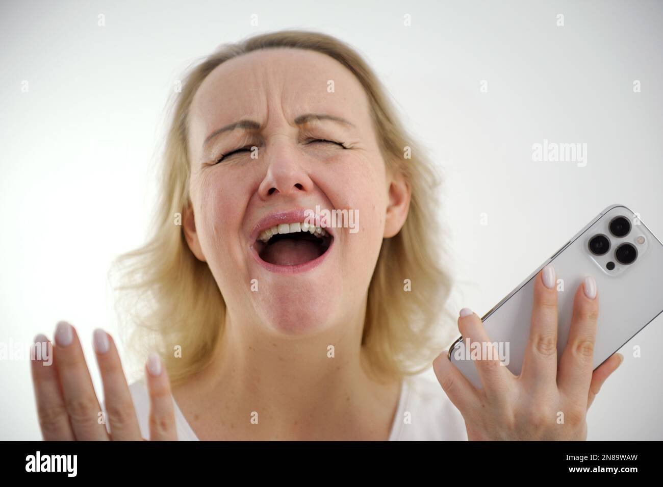 White Background Close Up Woman Screaming With Her Mouth Open Holding The Phone Raised Hands And