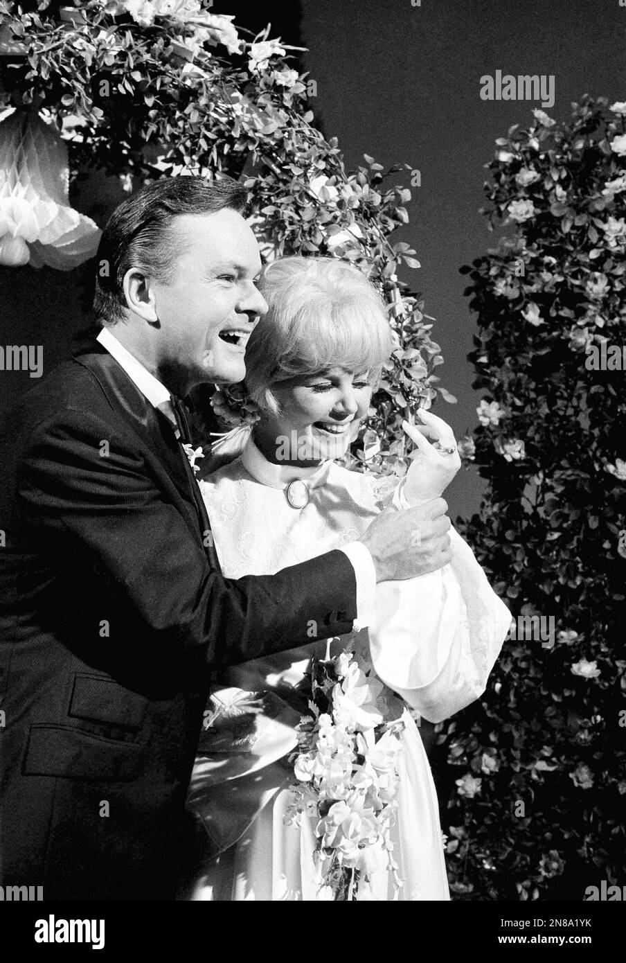 Bob Crane, star of the TV series "Hogan's Heroes", holds up his brides ...