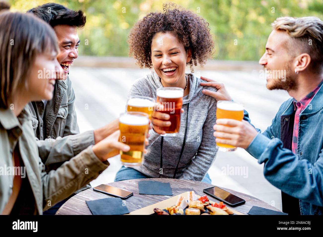 Multicultural friends drinking and toasting beer at city brewery bar ...