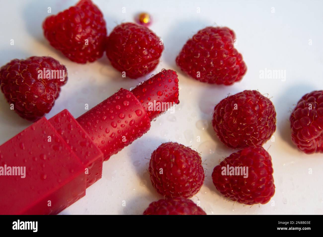 Bright red lipstick and ripe juicy raspberries on white background ...