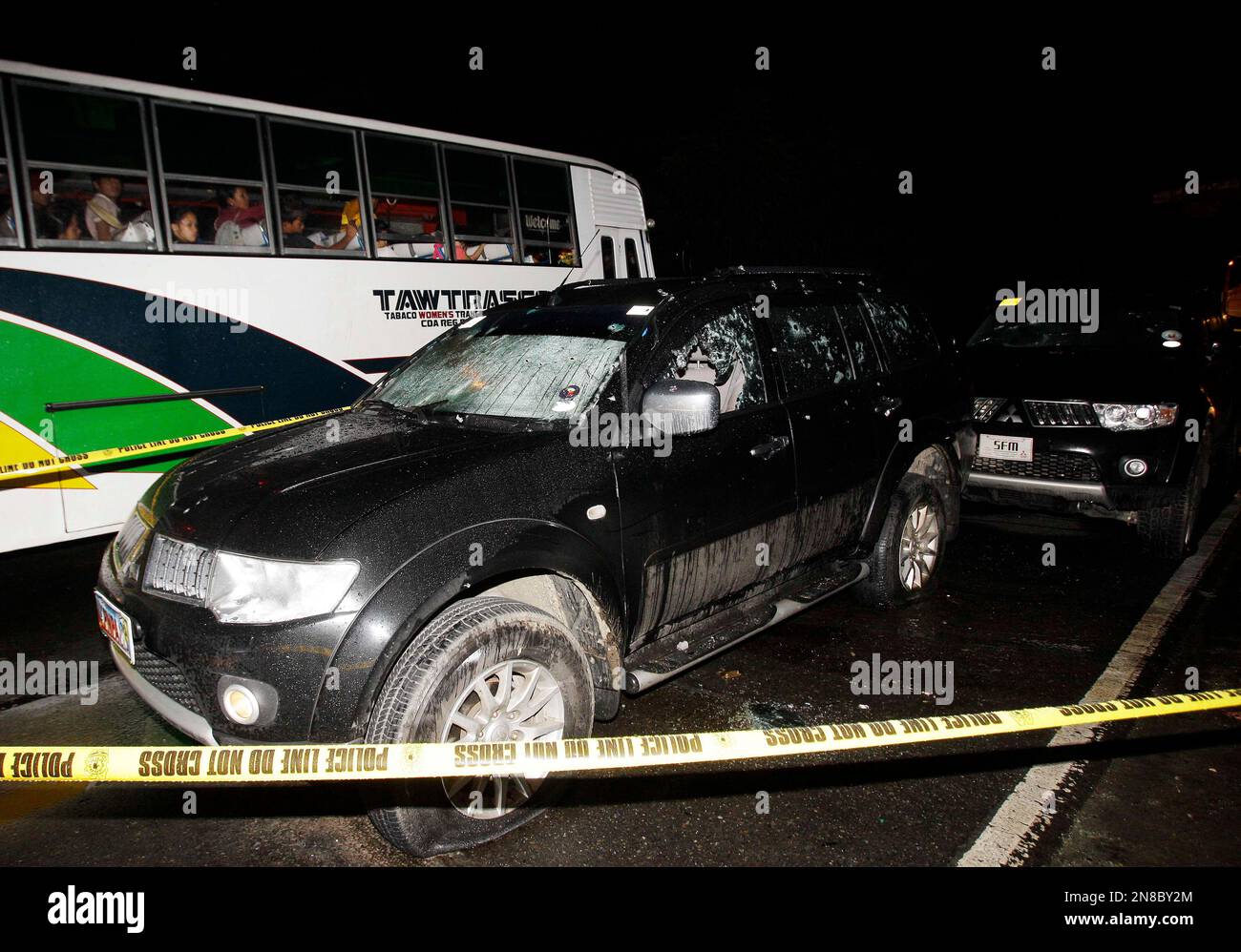 Passengers glance at the bullet-riddled vehicle of suspected criminals ...