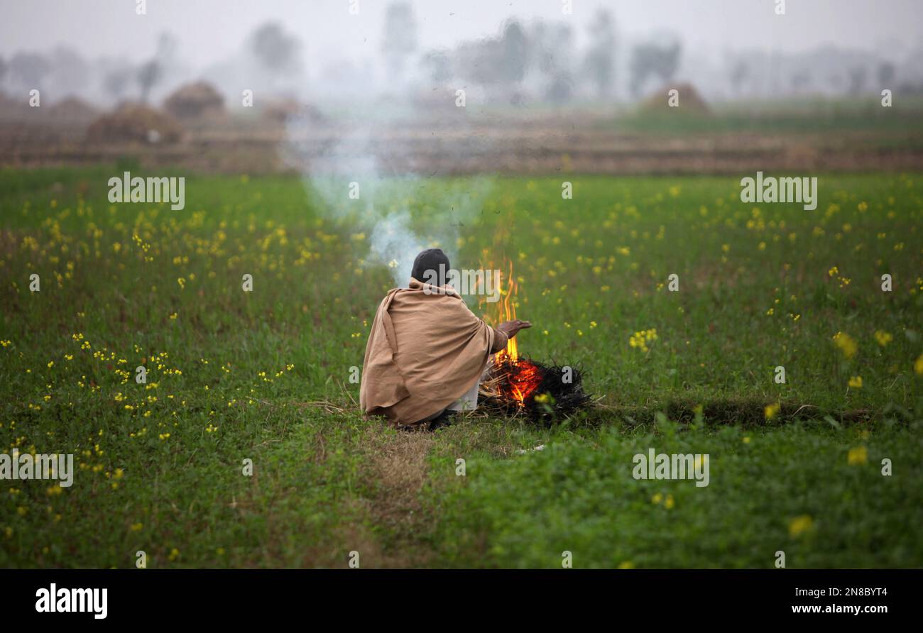 An Indian villager warms himself near a fire in a field at Gharana ...