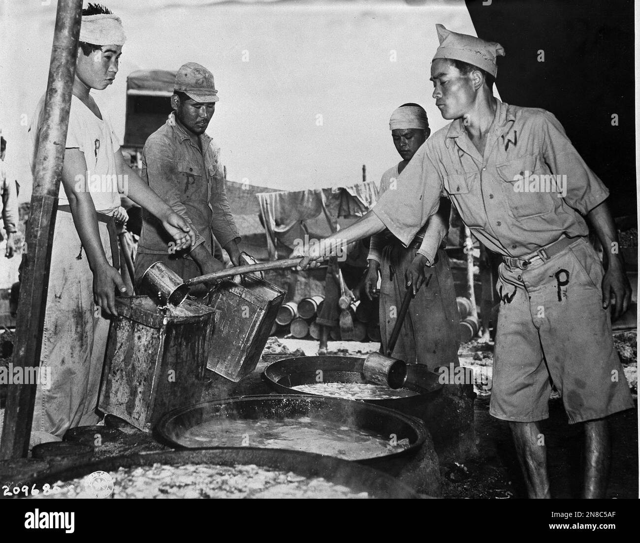 Japanese leaders of prisoner of war platoons line up with large cans to ...
