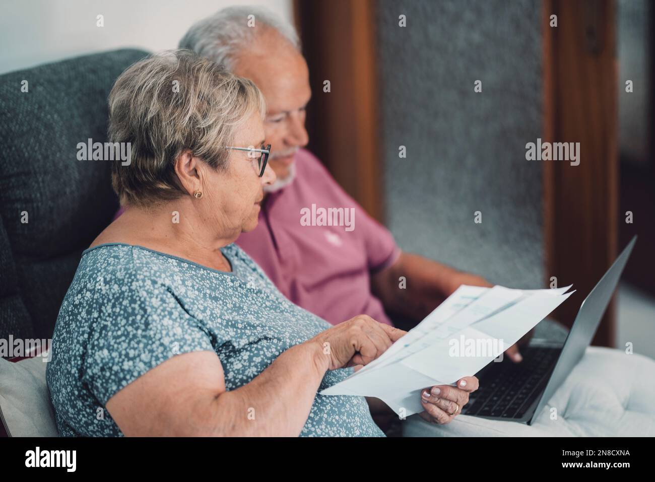SIde view of real senior couple at home paying bills online with ...
